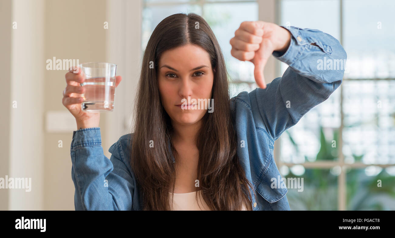 Young woman drinking glass of water at home with angry face, negative ...