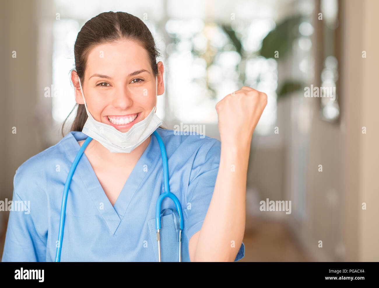 Young nurse woman wearing mask and stethoscope screaming proud and ...