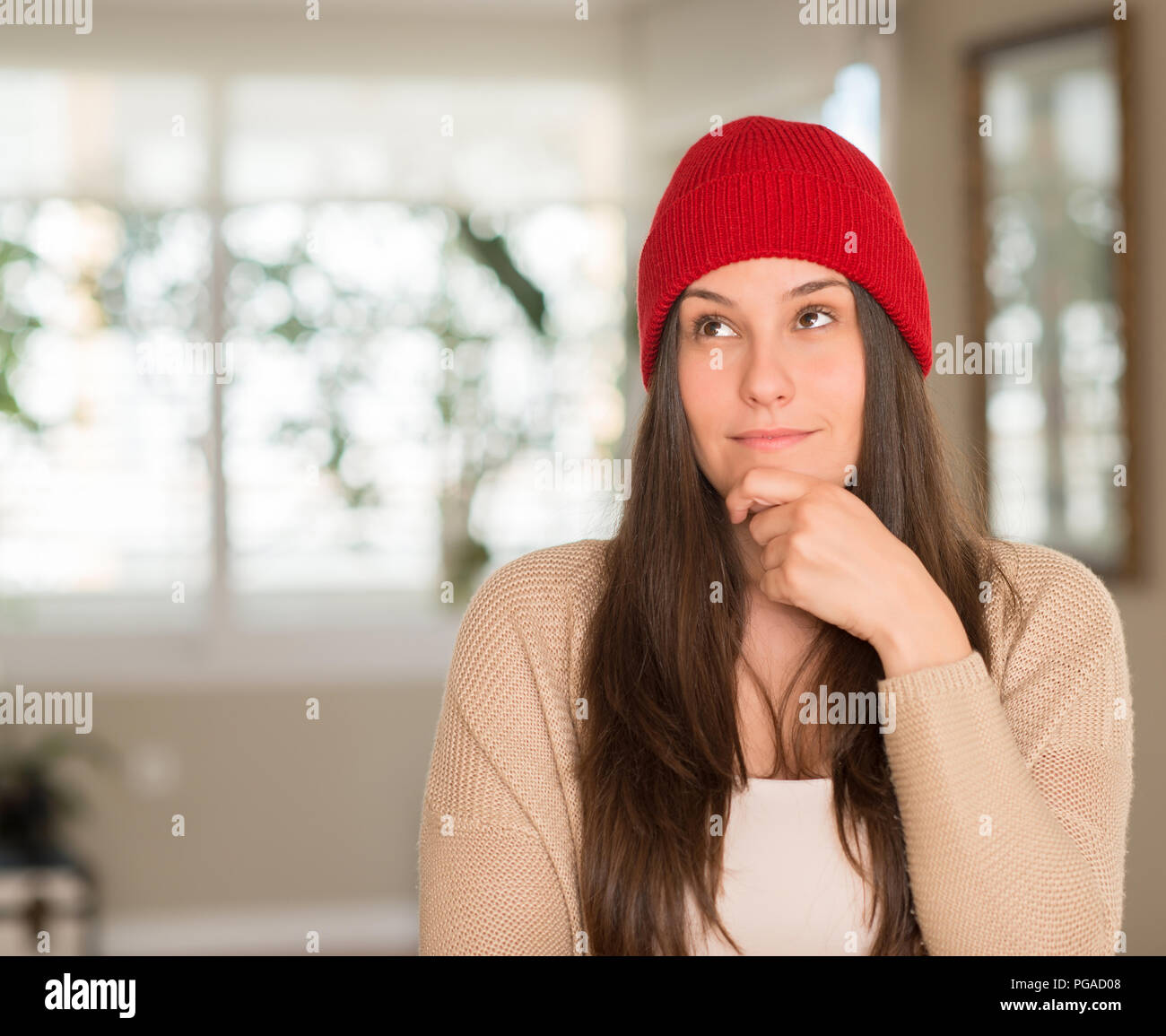 Young beautiful woman wearing red cap at home serious face thinking ...