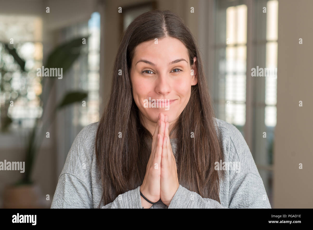 Young beautiful woman at home praying with hands together asking for ...
