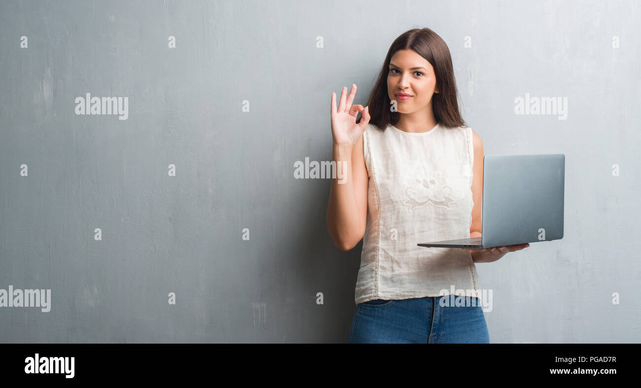 Young brunette woman over grunge grey wall using computer laptop doing ...