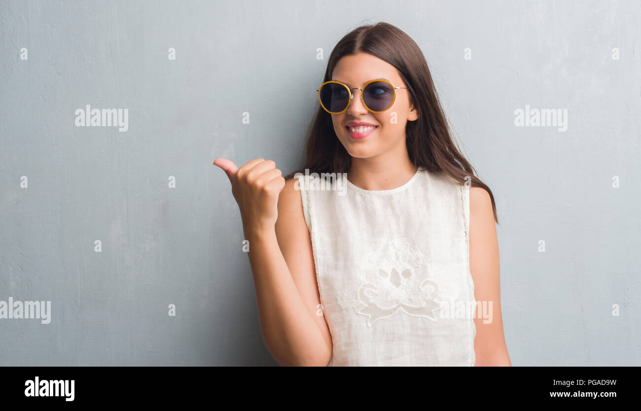 Young brunette woman over grunge grey wall wearing retro sunglasses ...