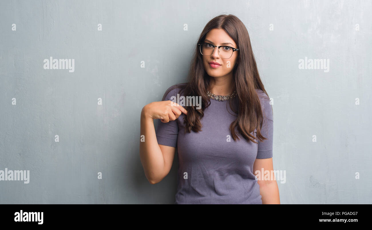 Young brunette woman over grunge grey wall wearing glasses with ...