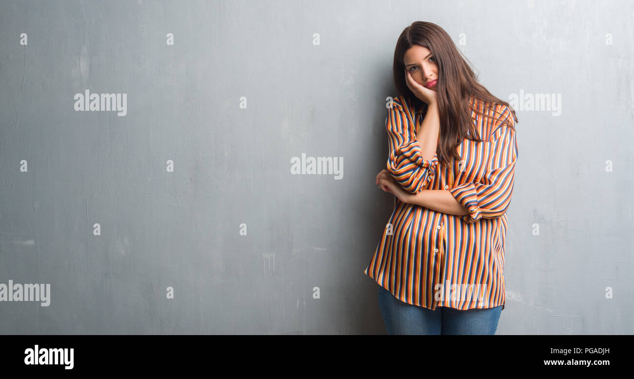 Young brunette woman over grunge grey wall thinking looking tired and ...