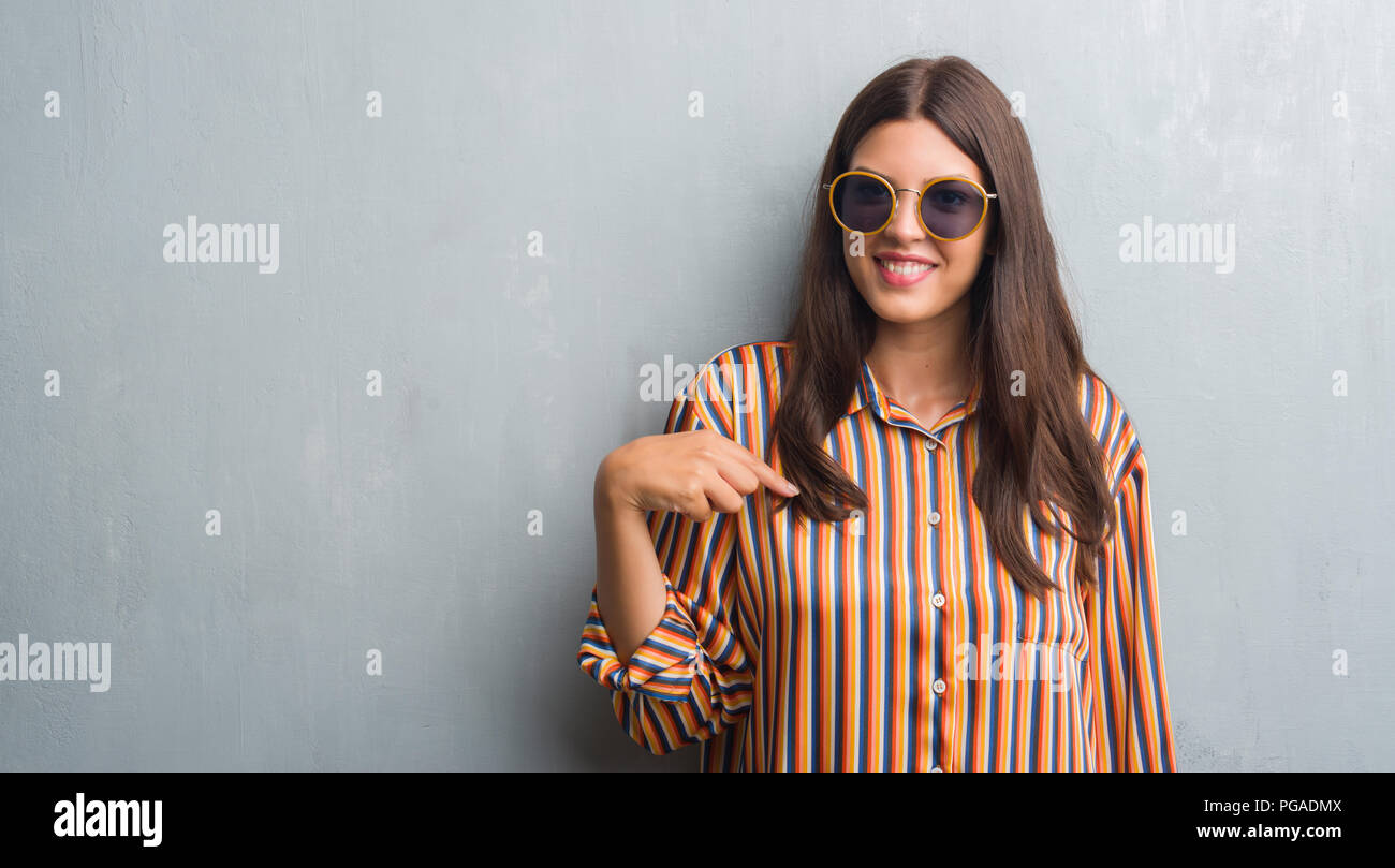Young brunette woman over grunge grey wall wearing retro sunglasses and ...