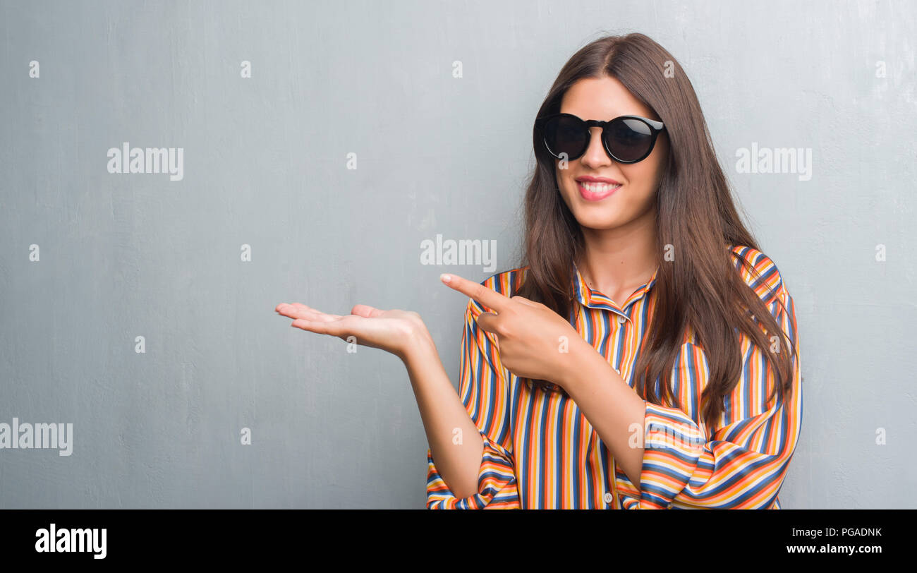 Young brunette woman over grunge grey wall wearing big sunglasses very ...