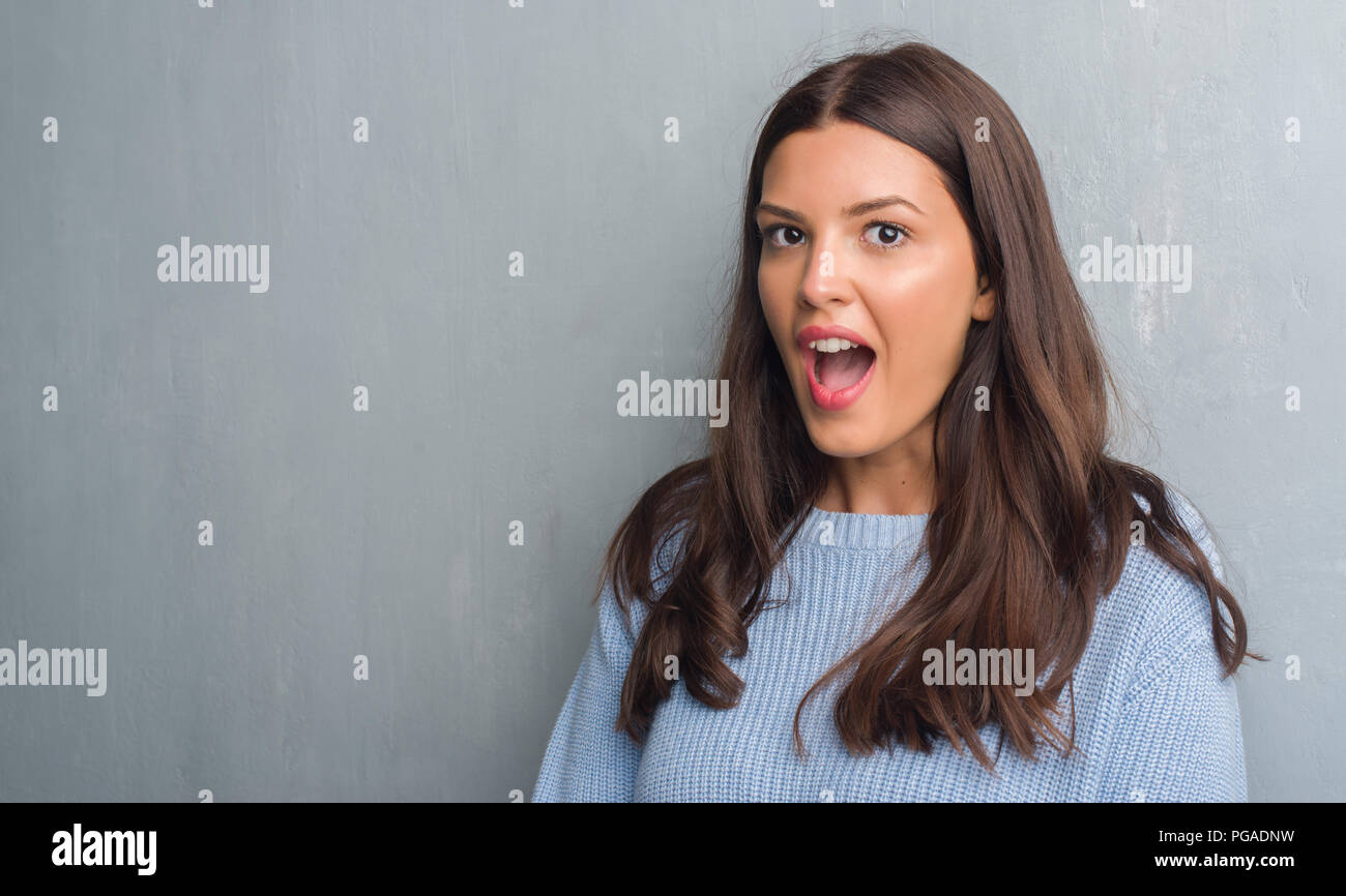 Young brunette woman over grunge grey wall scared in shock with a ...