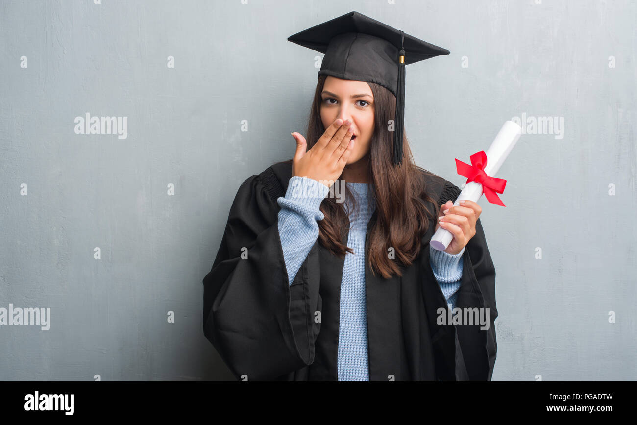 Young brunette woman over grunge grey wall wearing graduate uniform ...