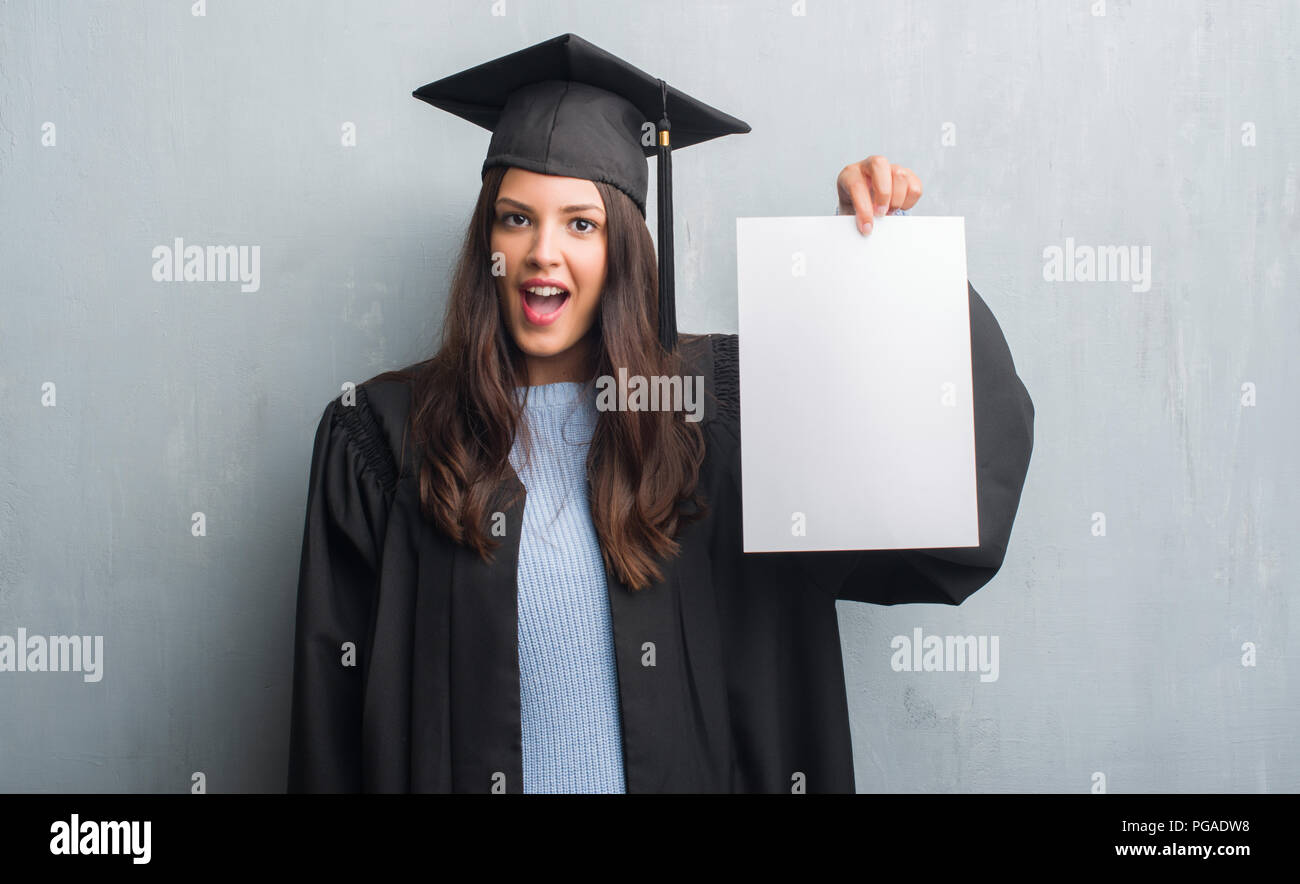 Young brunette woman over grunge grey wall wearing graduate uniform ...
