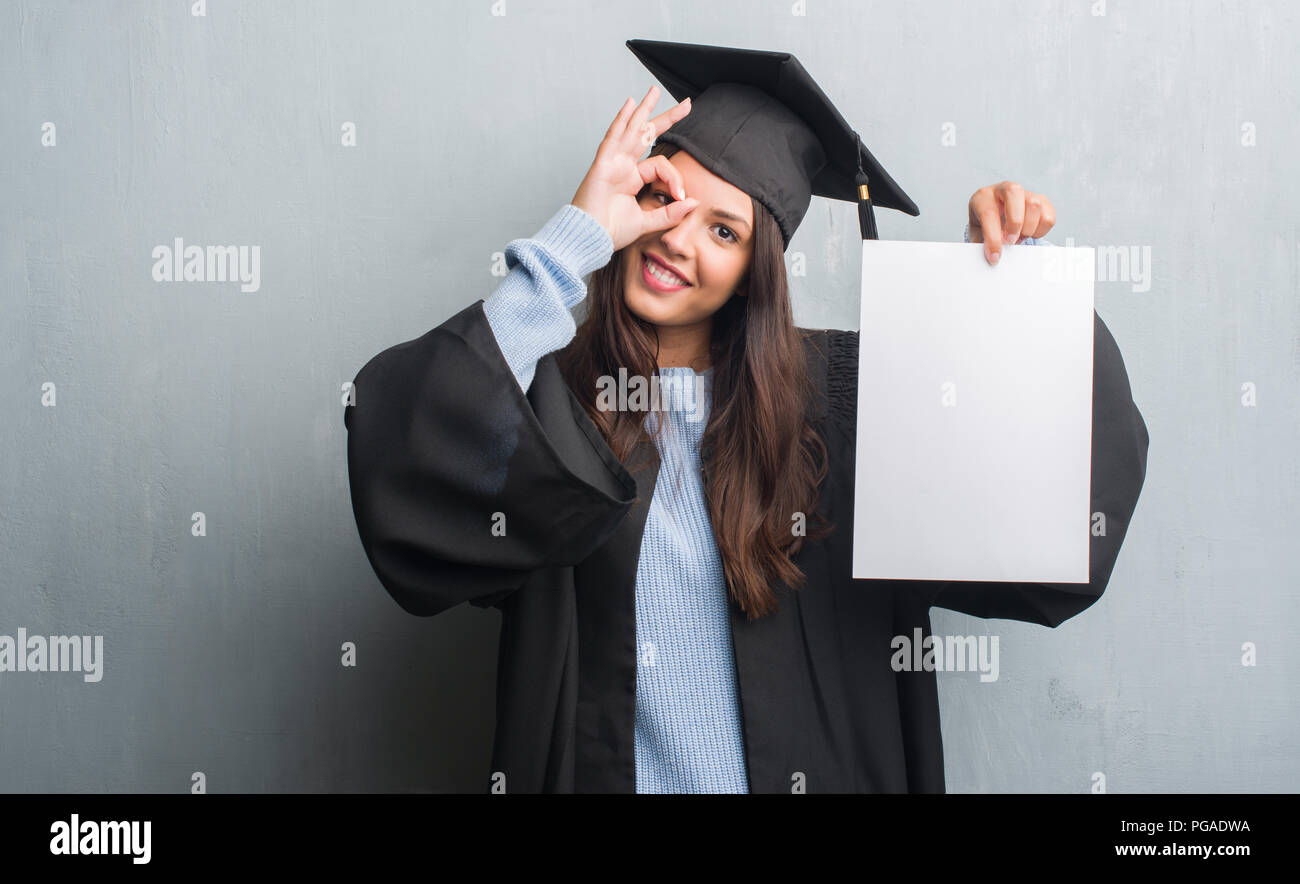 Young brunette woman over grunge grey wall wearing graduate uniform ...