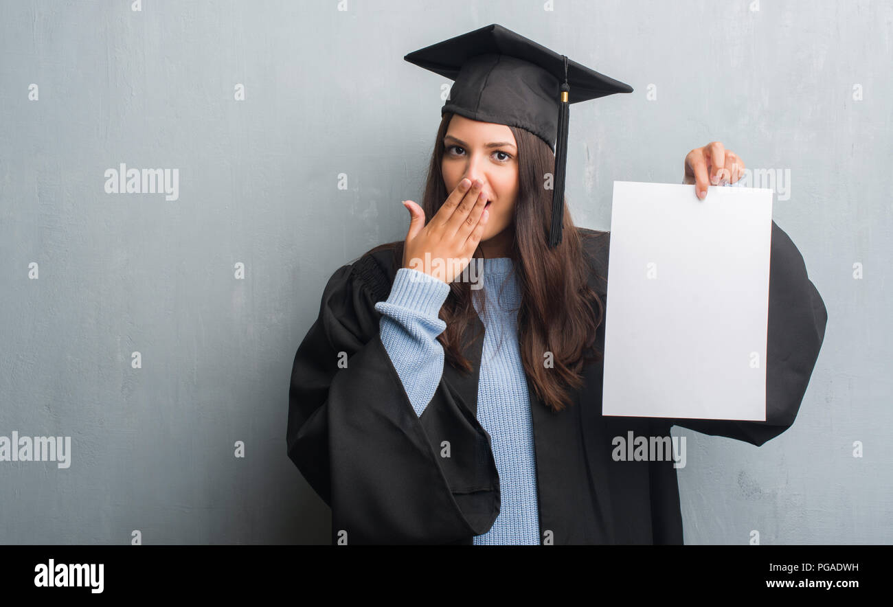 Young brunette woman over grunge grey wall wearing graduate uniform ...
