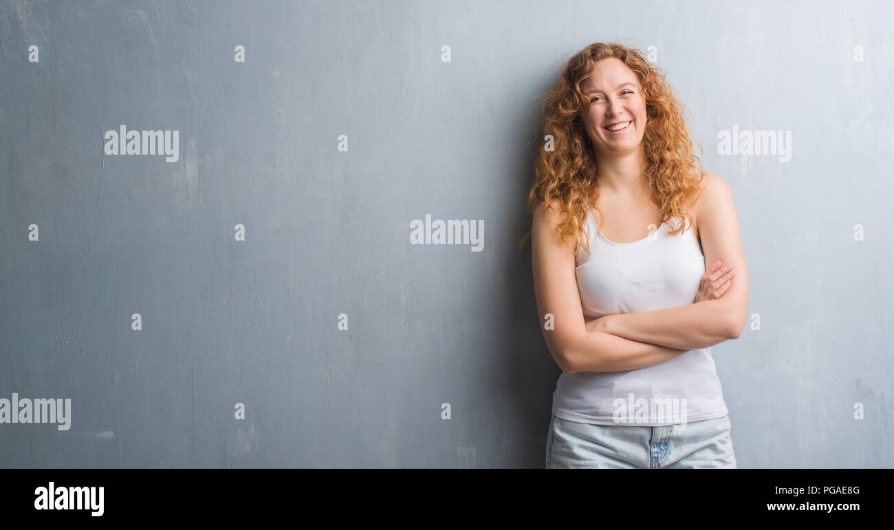 Young redhead woman over grey grunge wall with a happy face standing ...