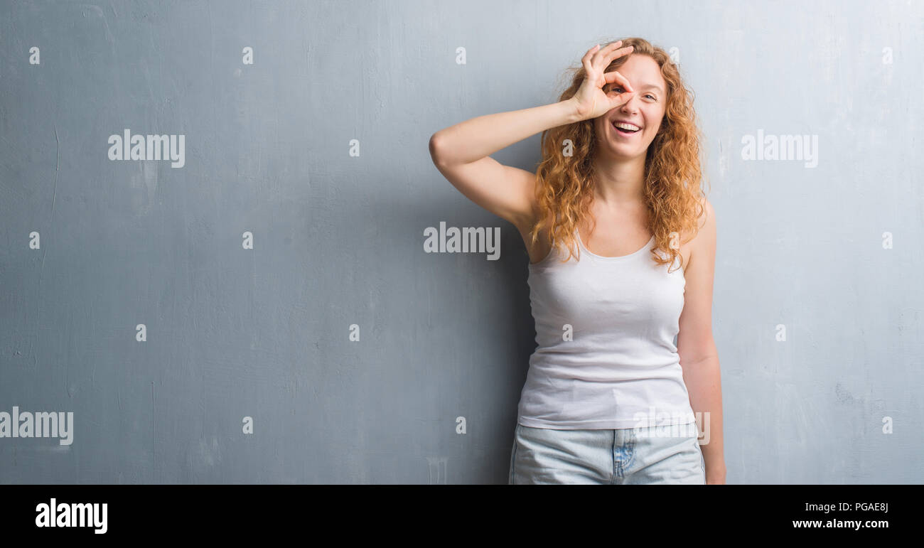 Young redhead woman over grey grunge wall with happy face smiling doing ...
