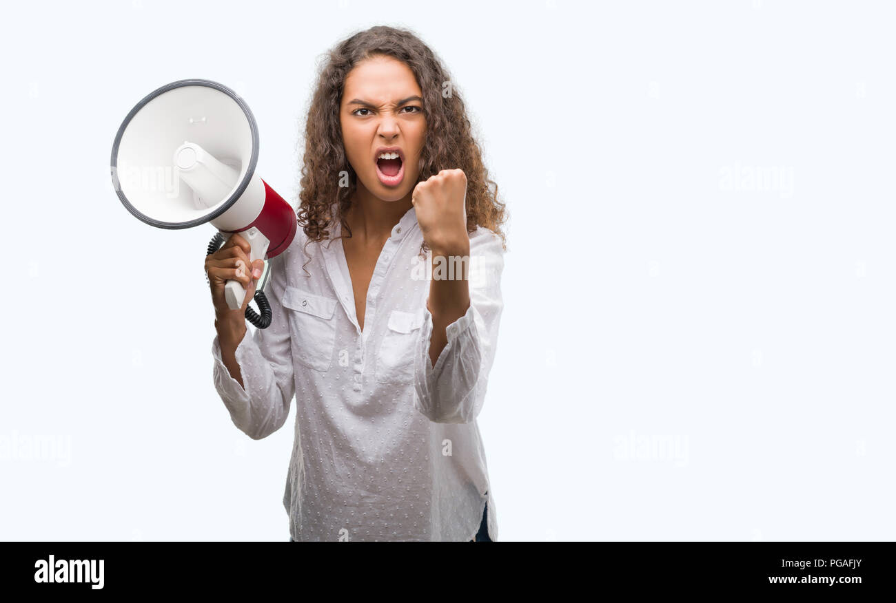 Young hispanic woman holding megaphone annoyed and frustrated shouting ...