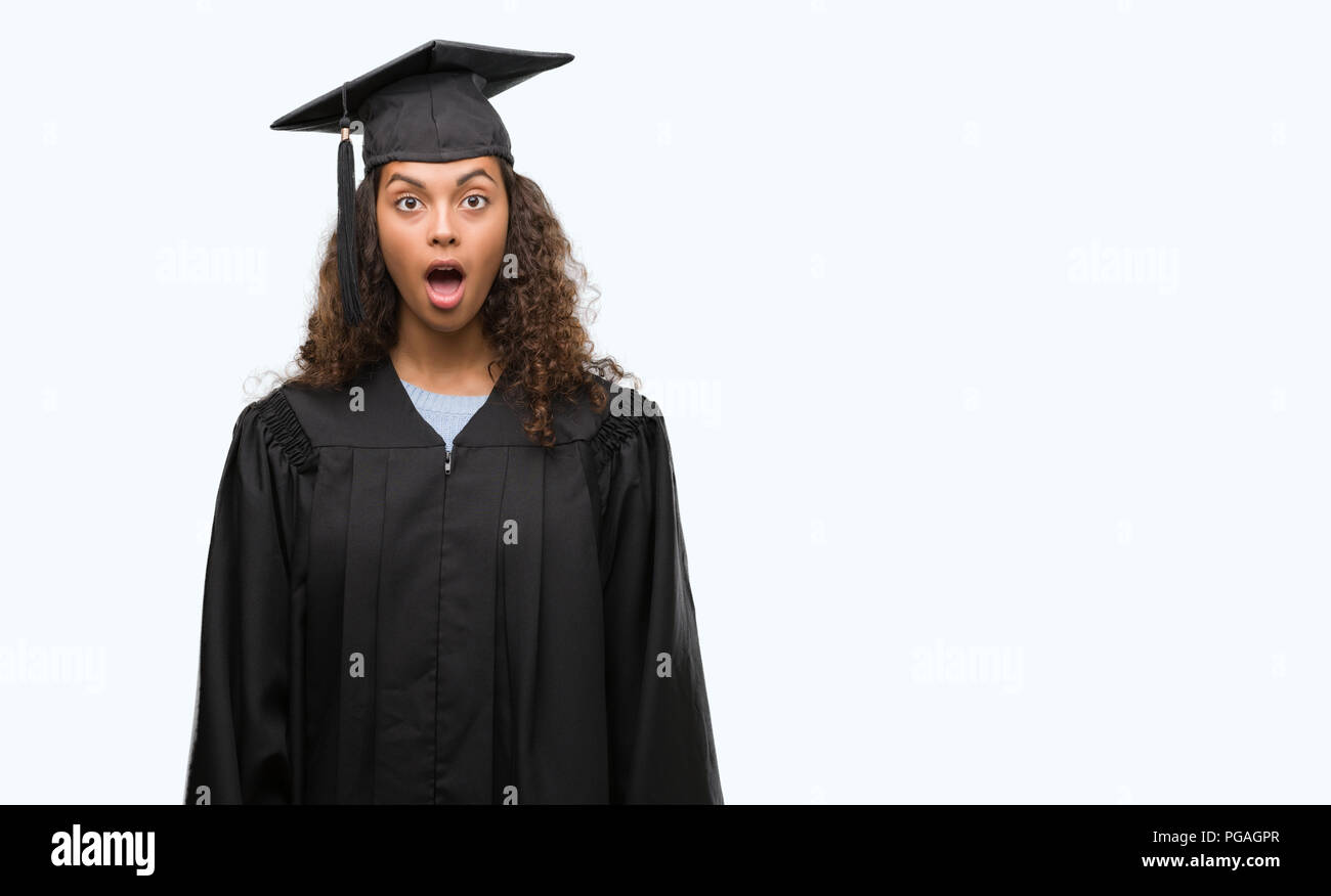 Young hispanic woman wearing graduation uniform scared in shock with a ...