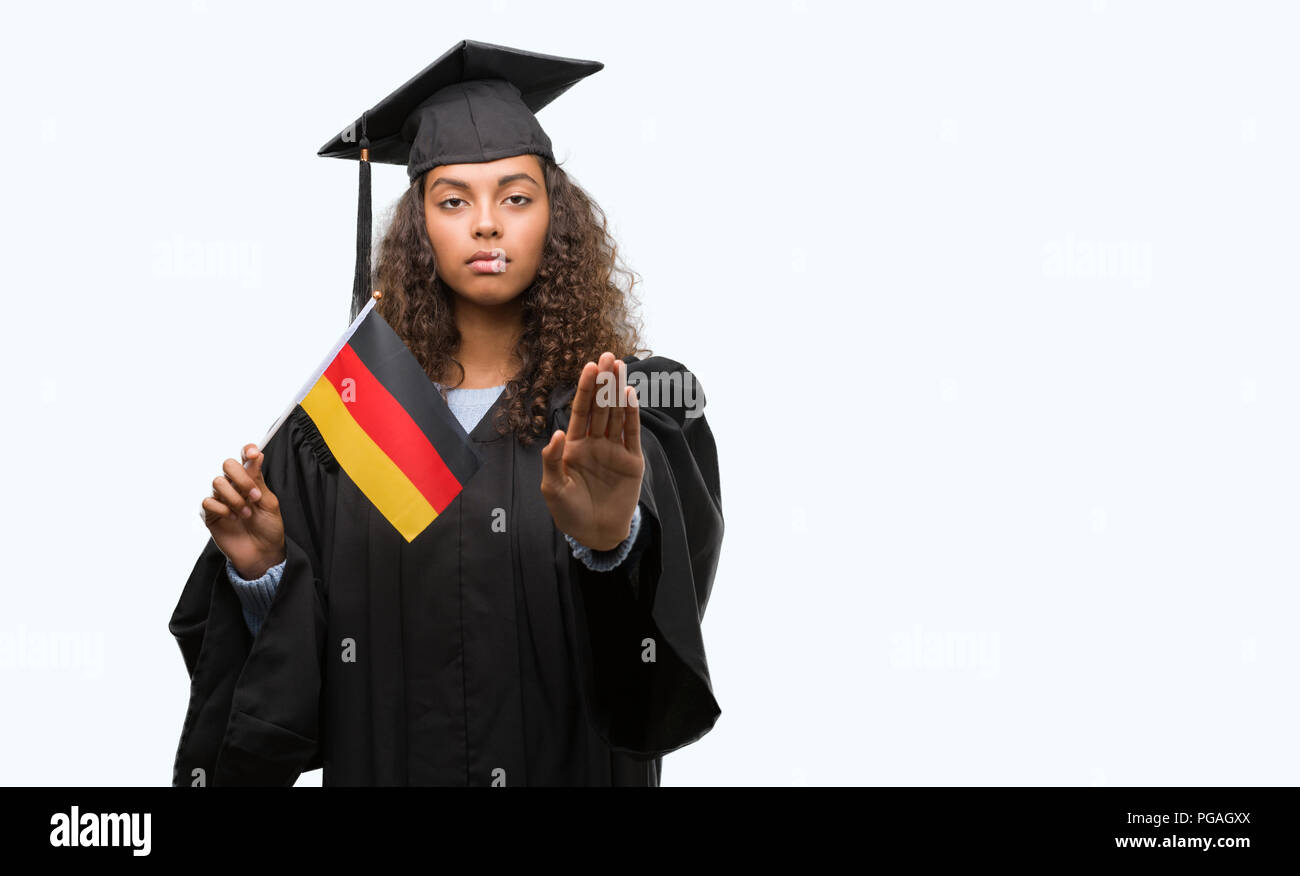 Young hispanic woman wearing graduation uniform holding flag of Germany ...