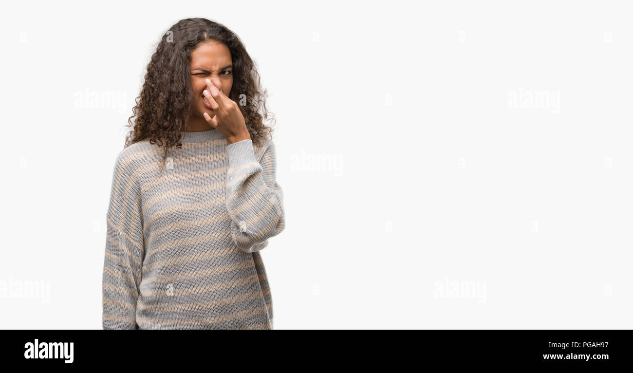 Beautiful young hispanic woman wearing stripes sweater smelling ...