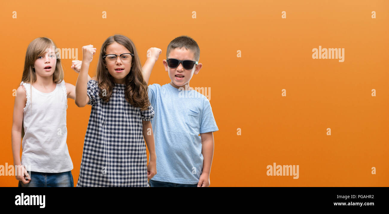 Group of boy and girls kids over orange background annoyed and ...
