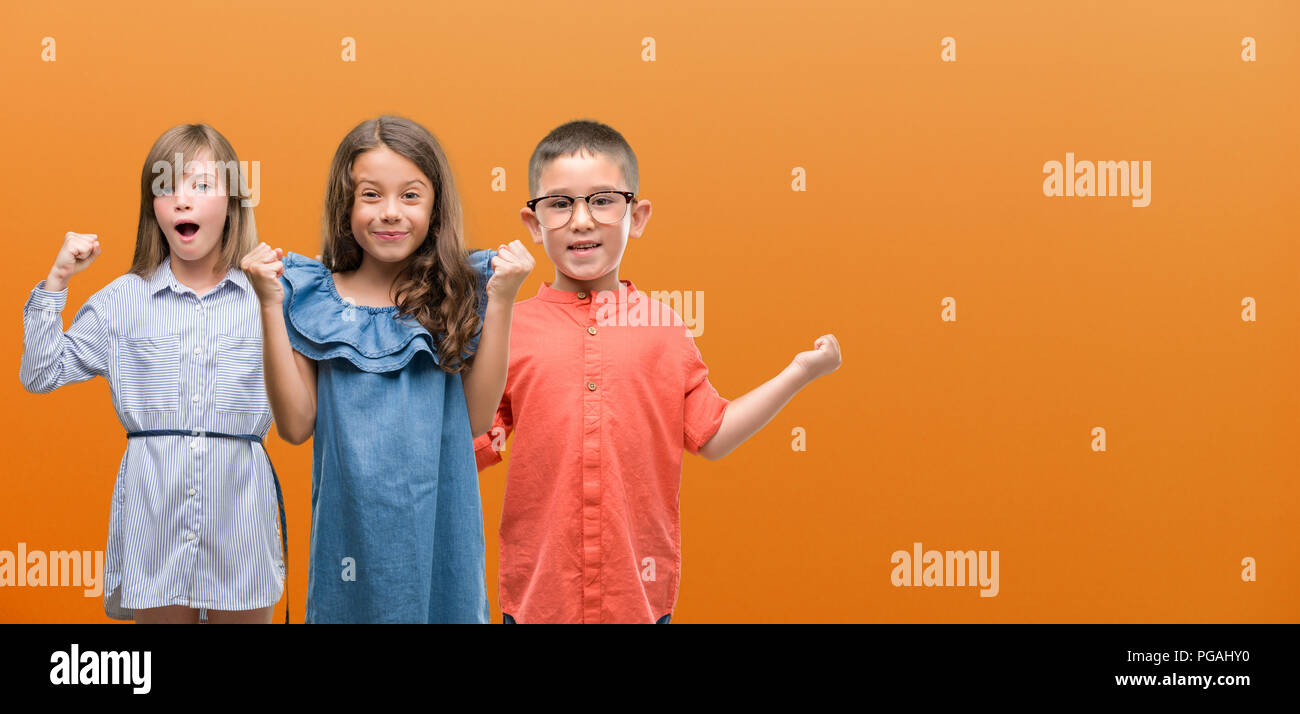 Group of boy and girls kids over orange background screaming proud and ...