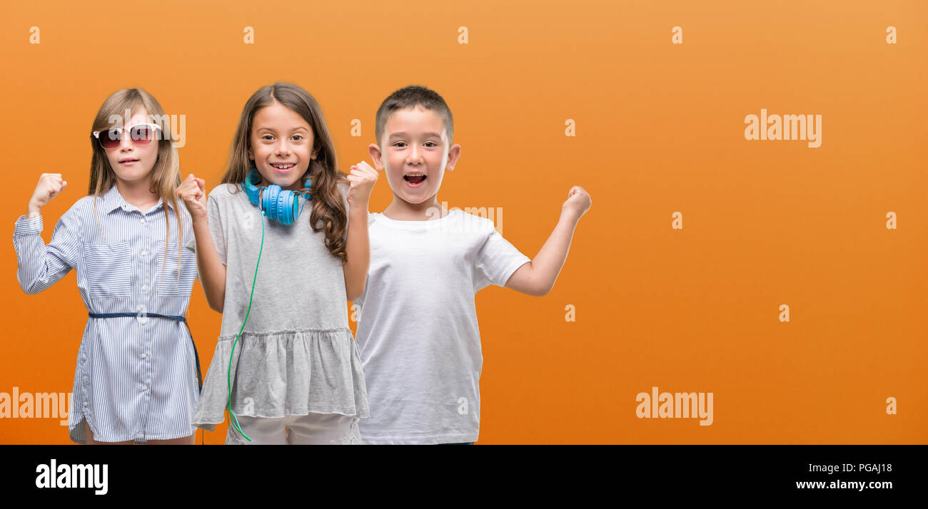 Group of boy and girls kids over orange background screaming proud and ...