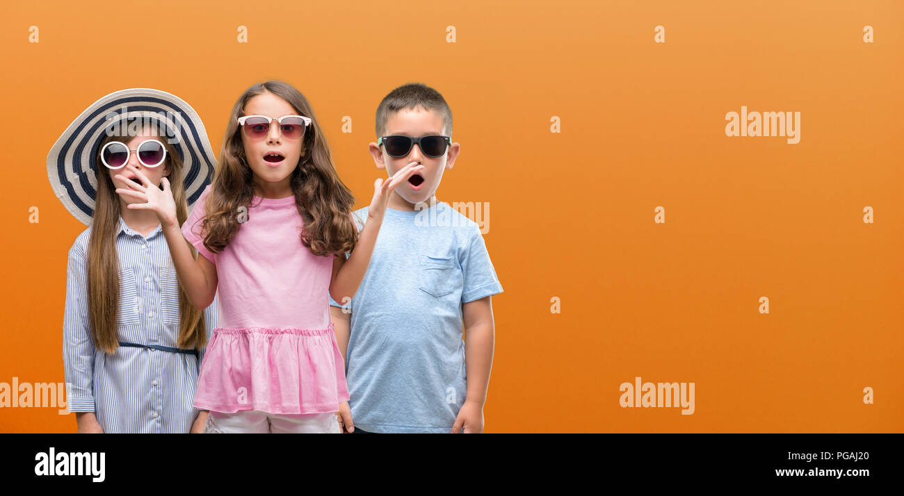 Group of boy and girls kids over orange background scared in shock with ...