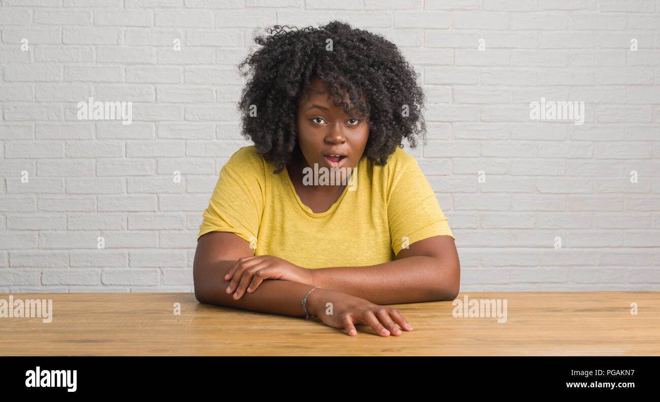 Young african american woman sitting on the table at home afraid and ...