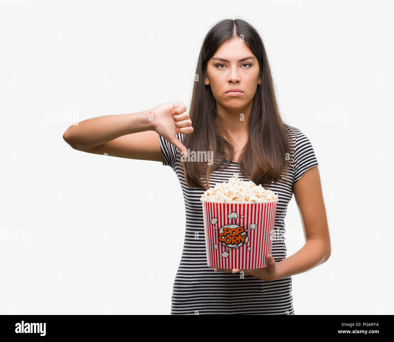 Young beautiful hispanic eating popcorn with angry face, negative sign ...