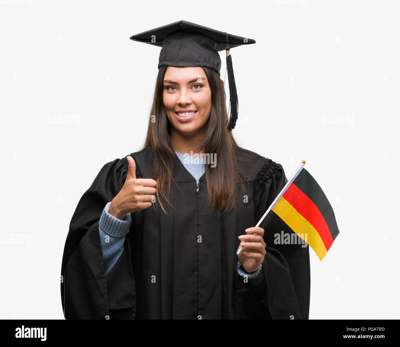 Young hispanic woman wearing graduated uniform holding flag of germany ...