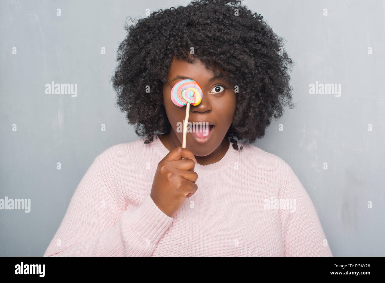 Young african american woman over grey grunge wall eating lollipop ...