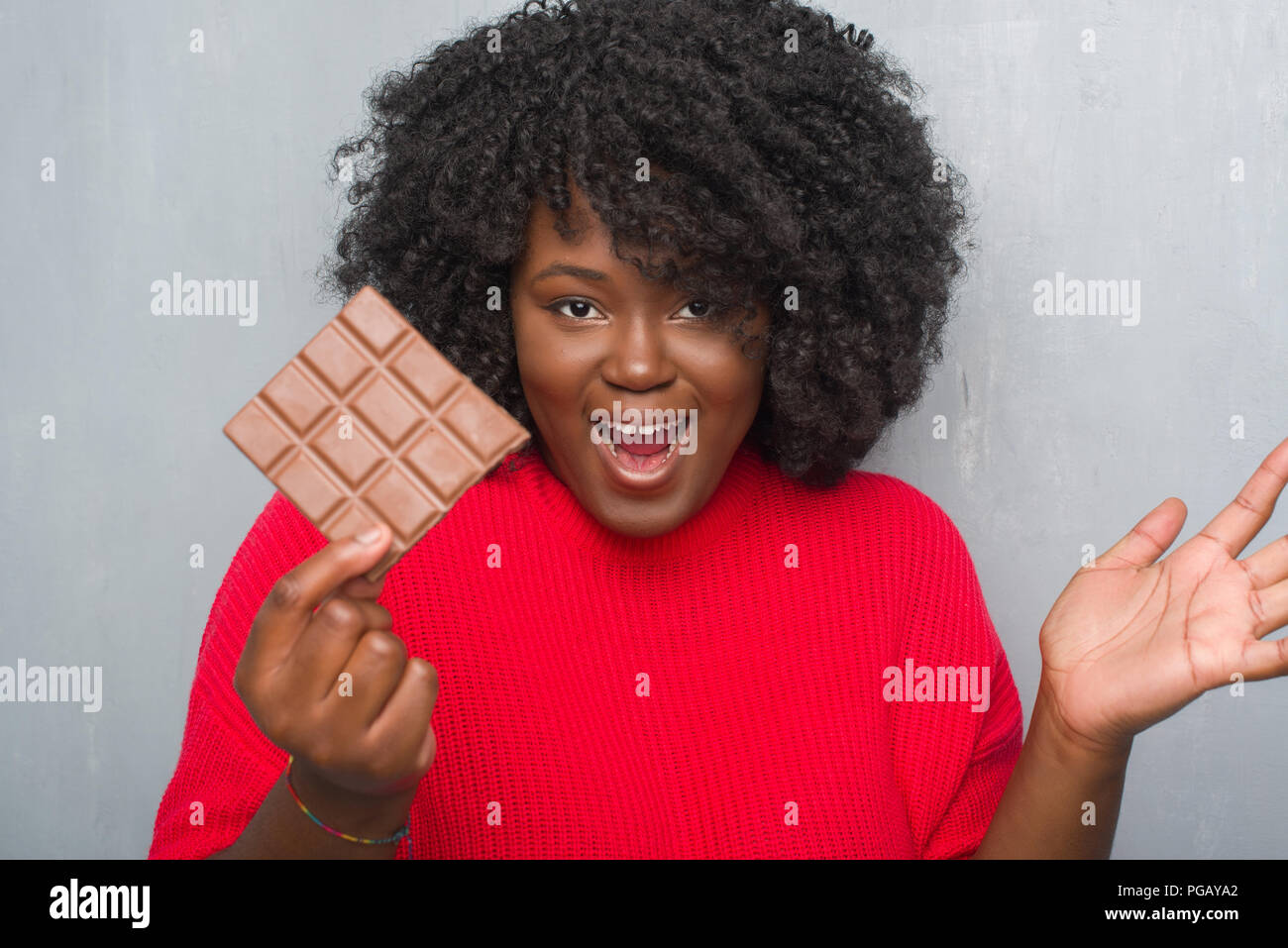 Young african american woman over grey grunge wall eating a chocolate ...