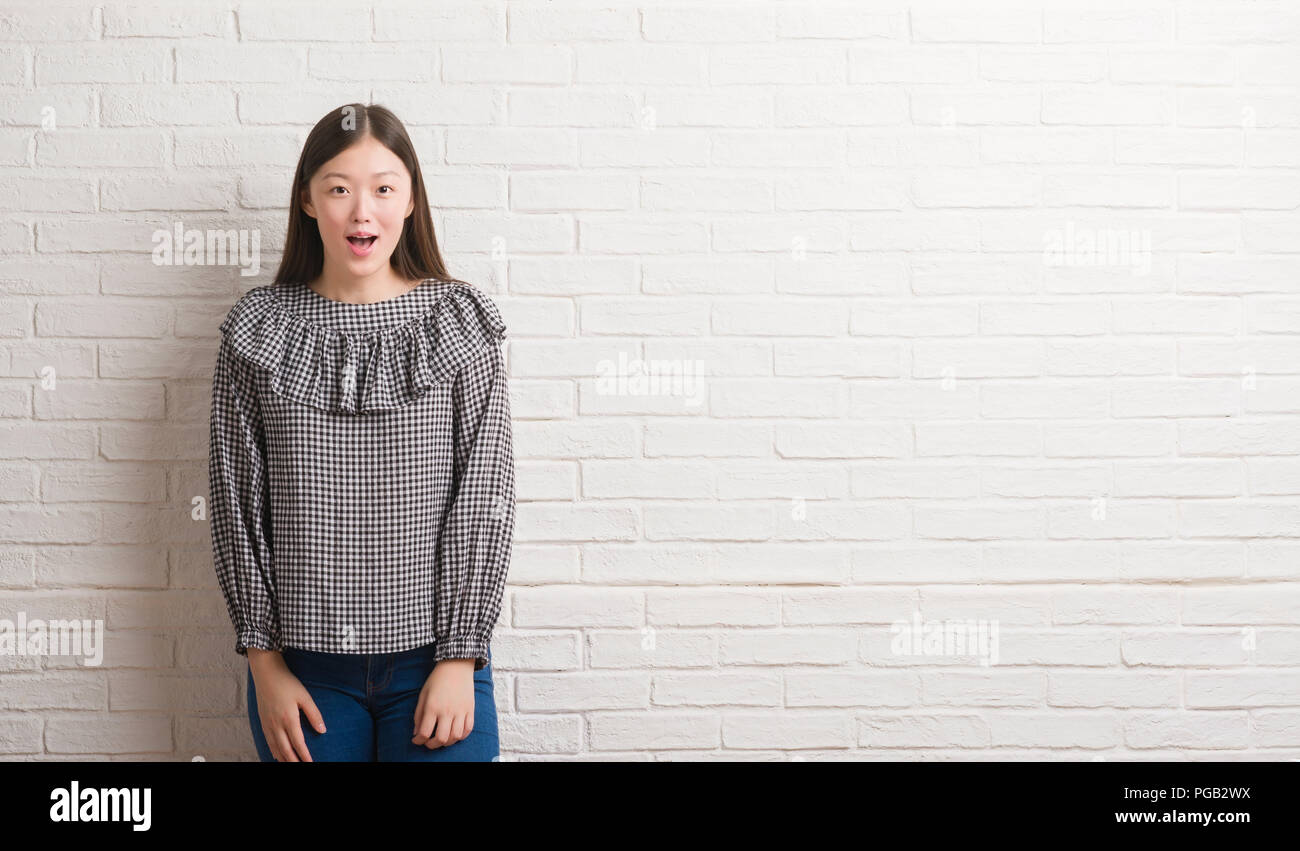 Young Chinese woman over brick wall scared in shock with a surprise ...