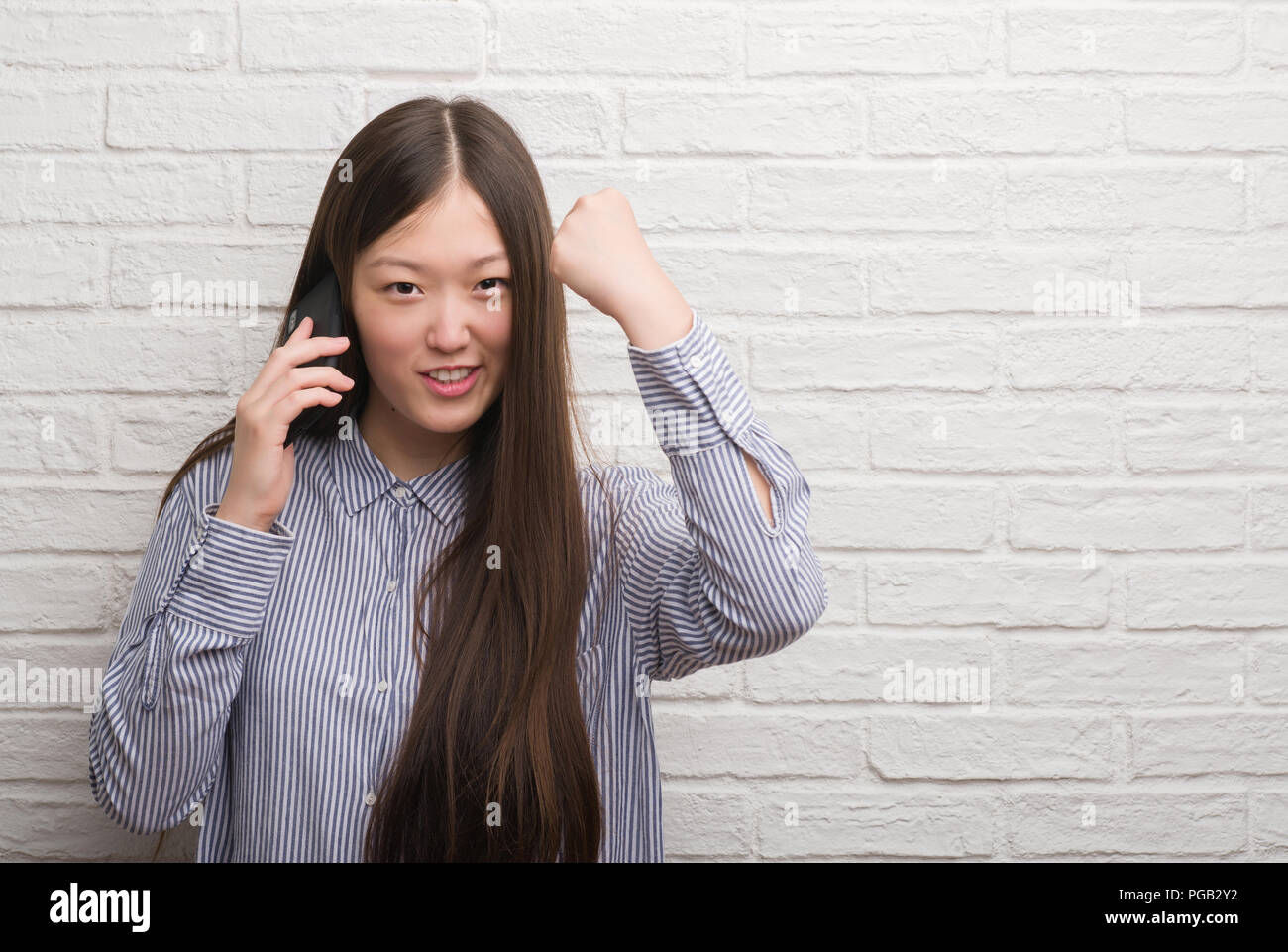 Young Chinese woman over brick wall talking on the phone annoyed and ...