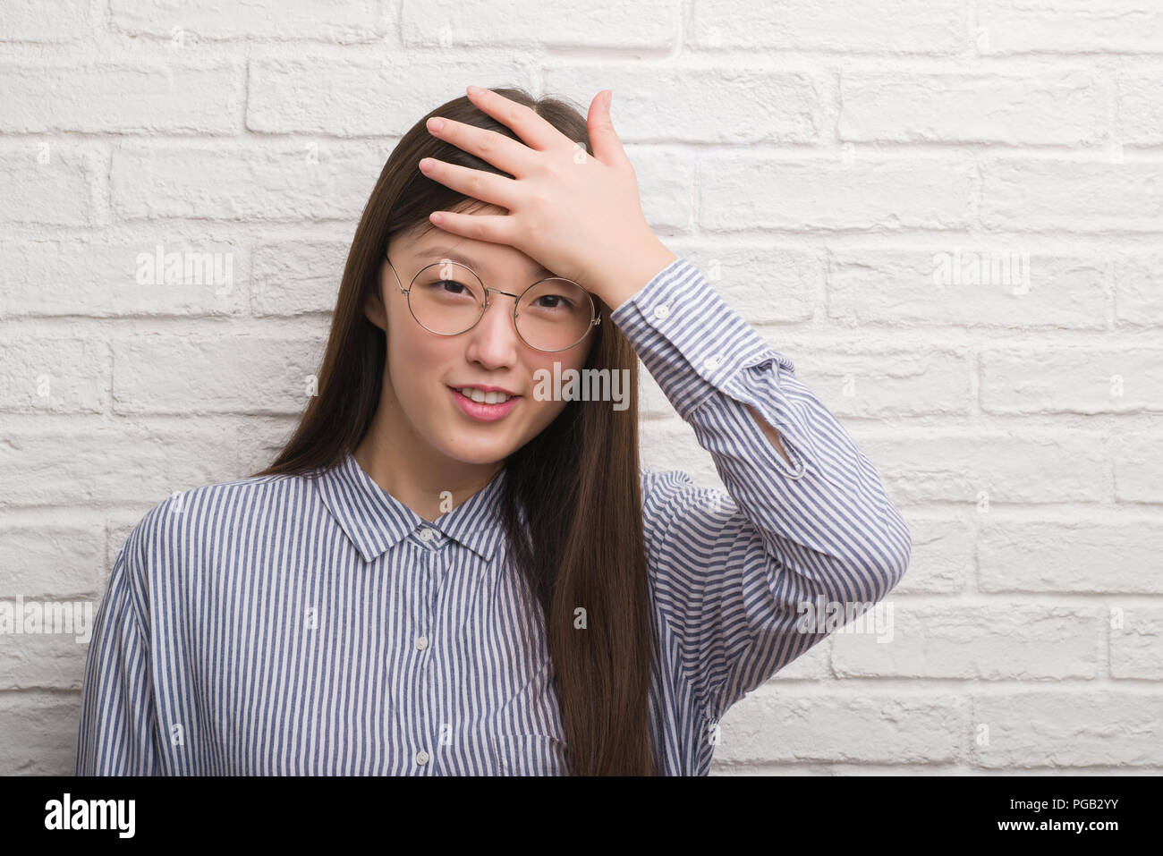 Young Chinese business woman over brick wall stressed with hand on head ...