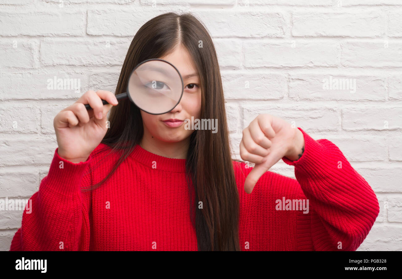 Young Chinese woman over brick wall looking through magnifying glass ...