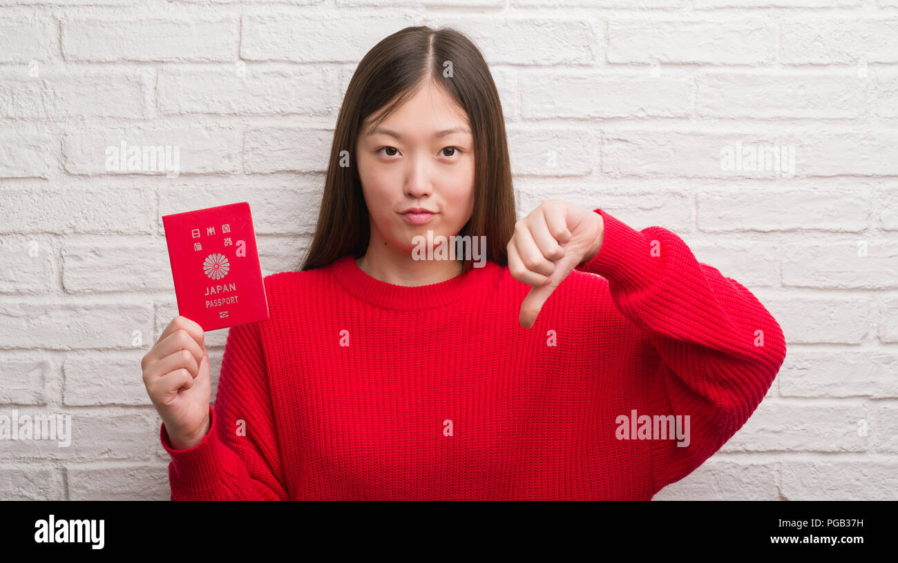 Young Chinese woman over brick wall holding passport of Japan with ...