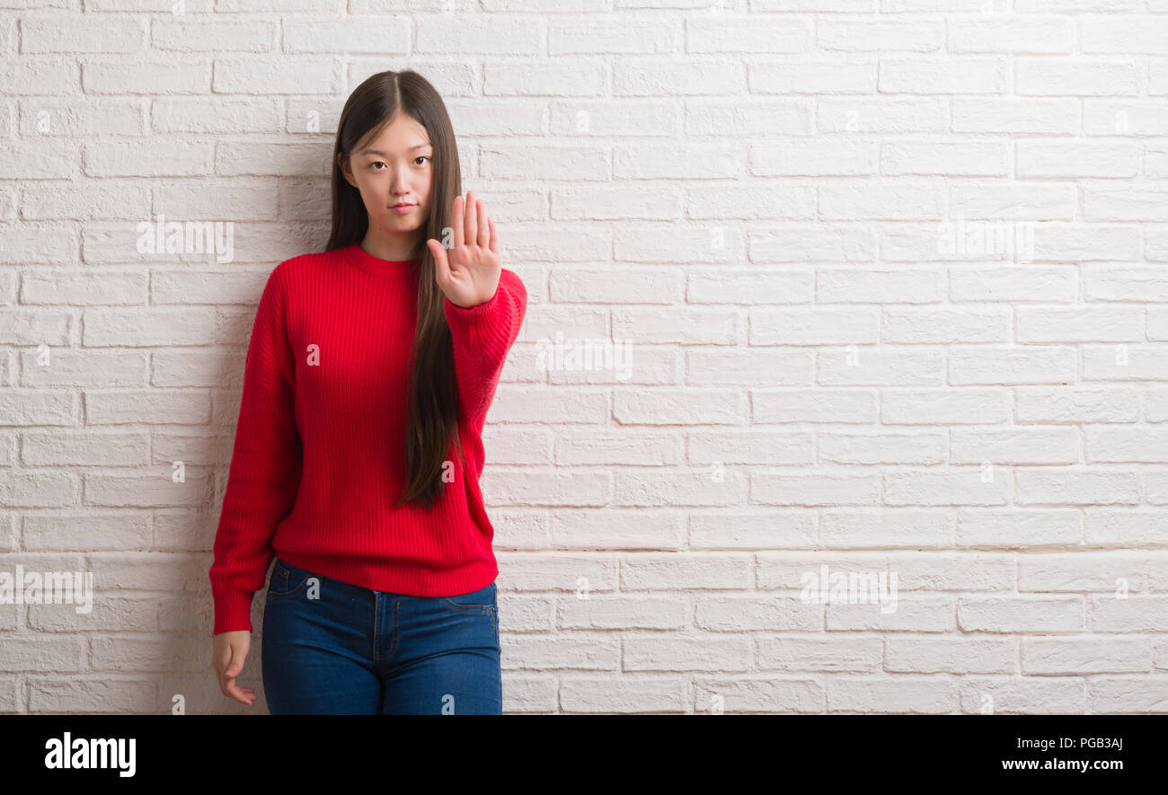 Young Chinese woman over brick wall doing stop sing with palm of the ...