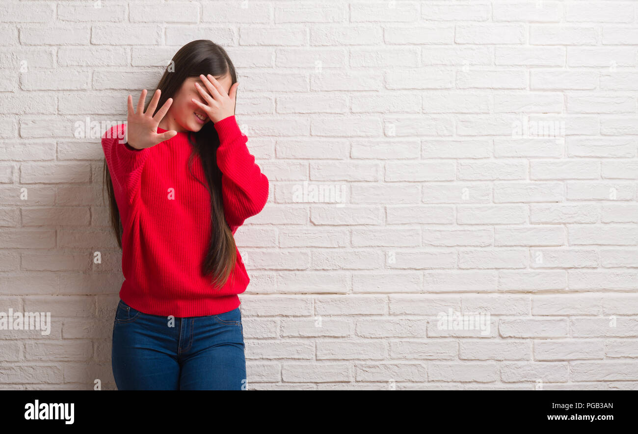 Young Chinese woman over brick wall covering eyes with hands and doing ...