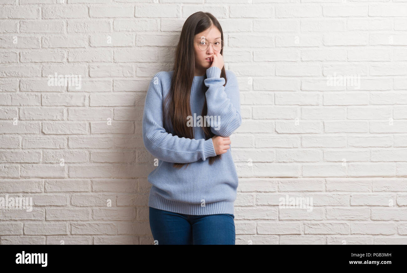 Young Chinise woman over white brick wall looking stressed and nervous ...