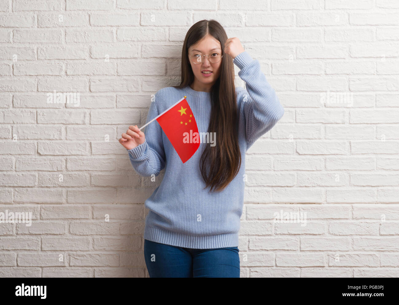 Young Chinese woman over brick wall holding flag of China annoyed and ...