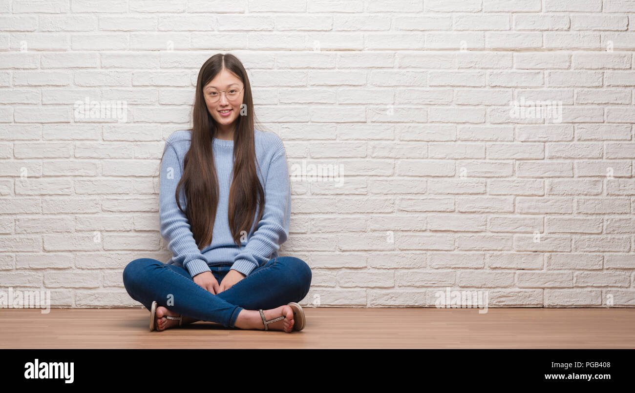 Young Chinese woman sitting on the floor over brick wall with a happy ...