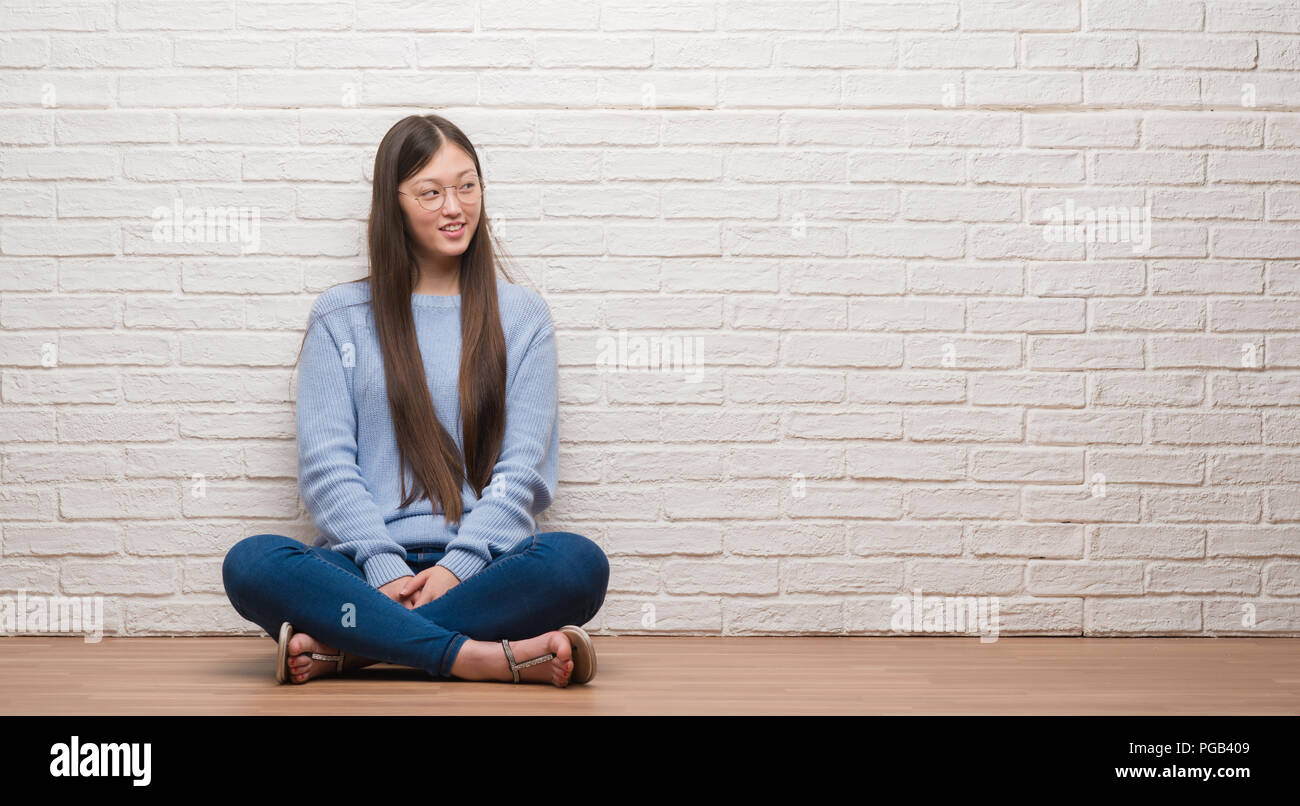 Young Chinese woman sitting on the floor over brick wall smiling ...