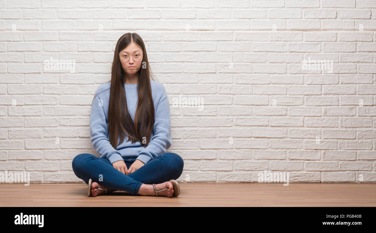 Young Chinese woman sitting on the floor over brick wall depressed and ...
