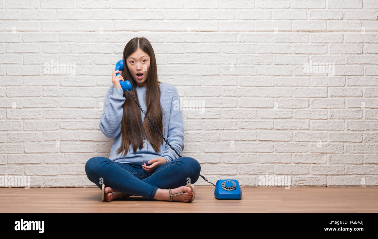 Young Chinese woman calling using vintage telephone scared in shock ...