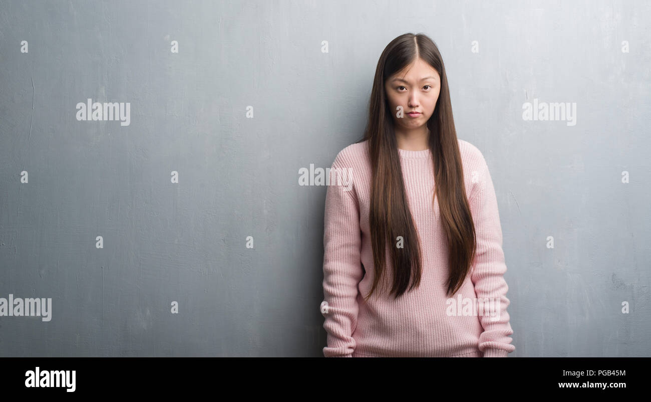 Young Chinese woman over grey wall depressed and worry for distress ...