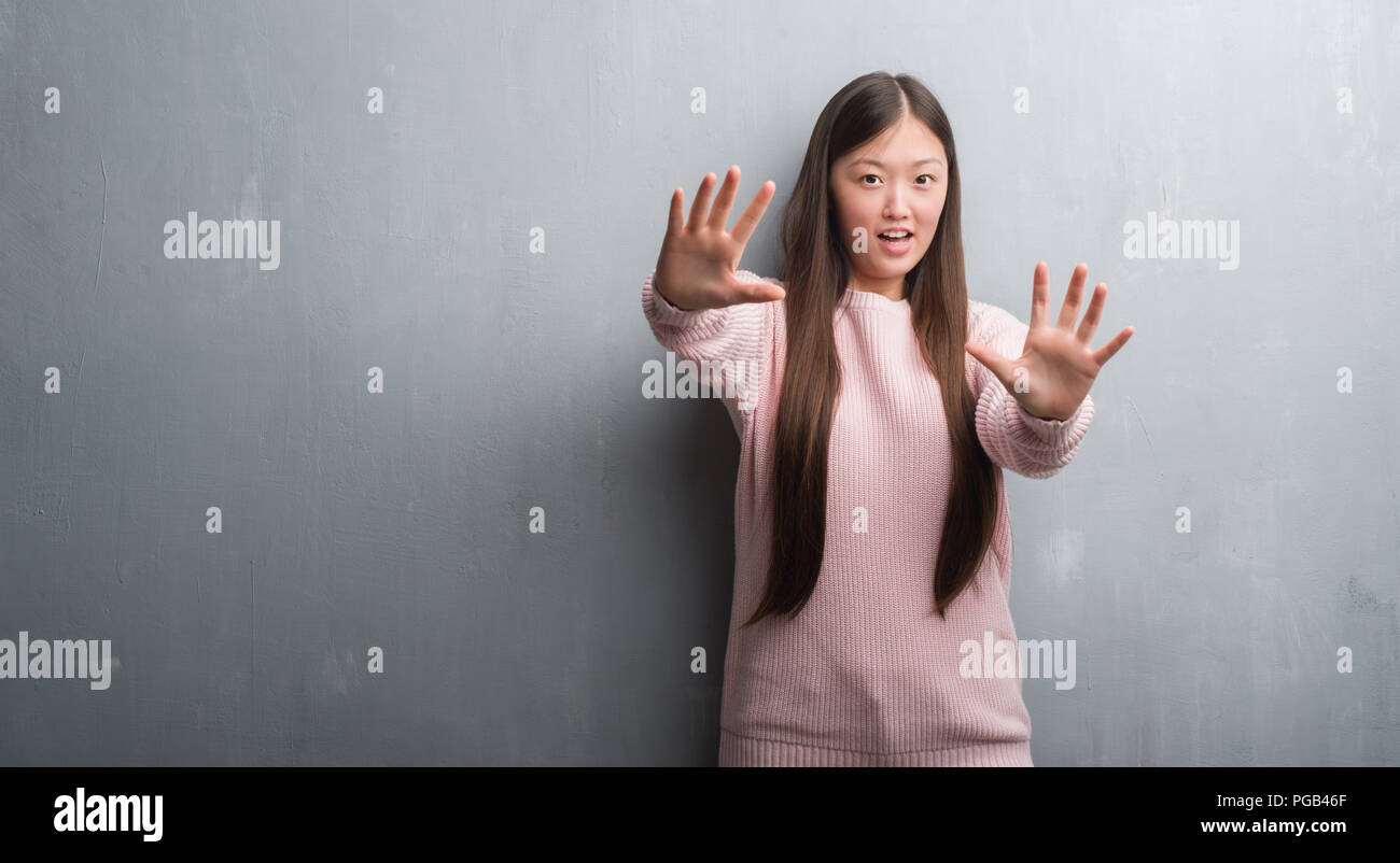 Young Chinese woman over grey wall afraid and terrified with fear ...