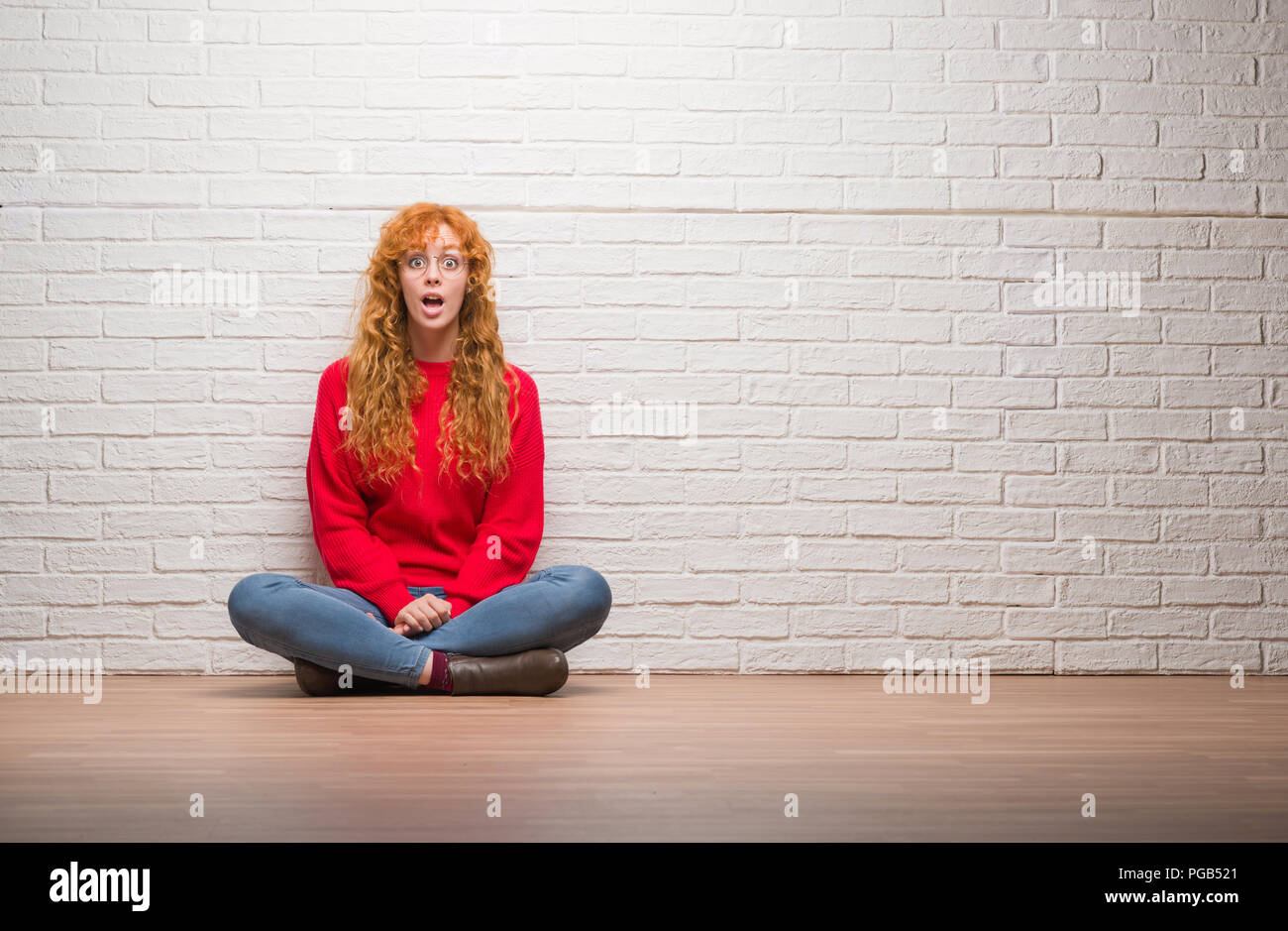 Young Redhead Woman Sitting Over Brick Wall Afraid And Shocked With