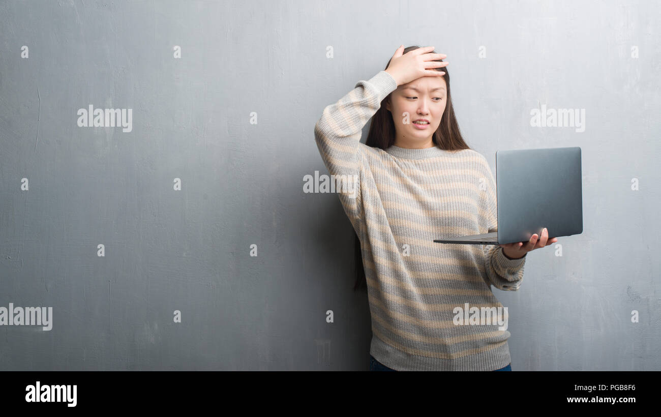 Young Chinese woman over grey wall using computer laptop stressed with ...