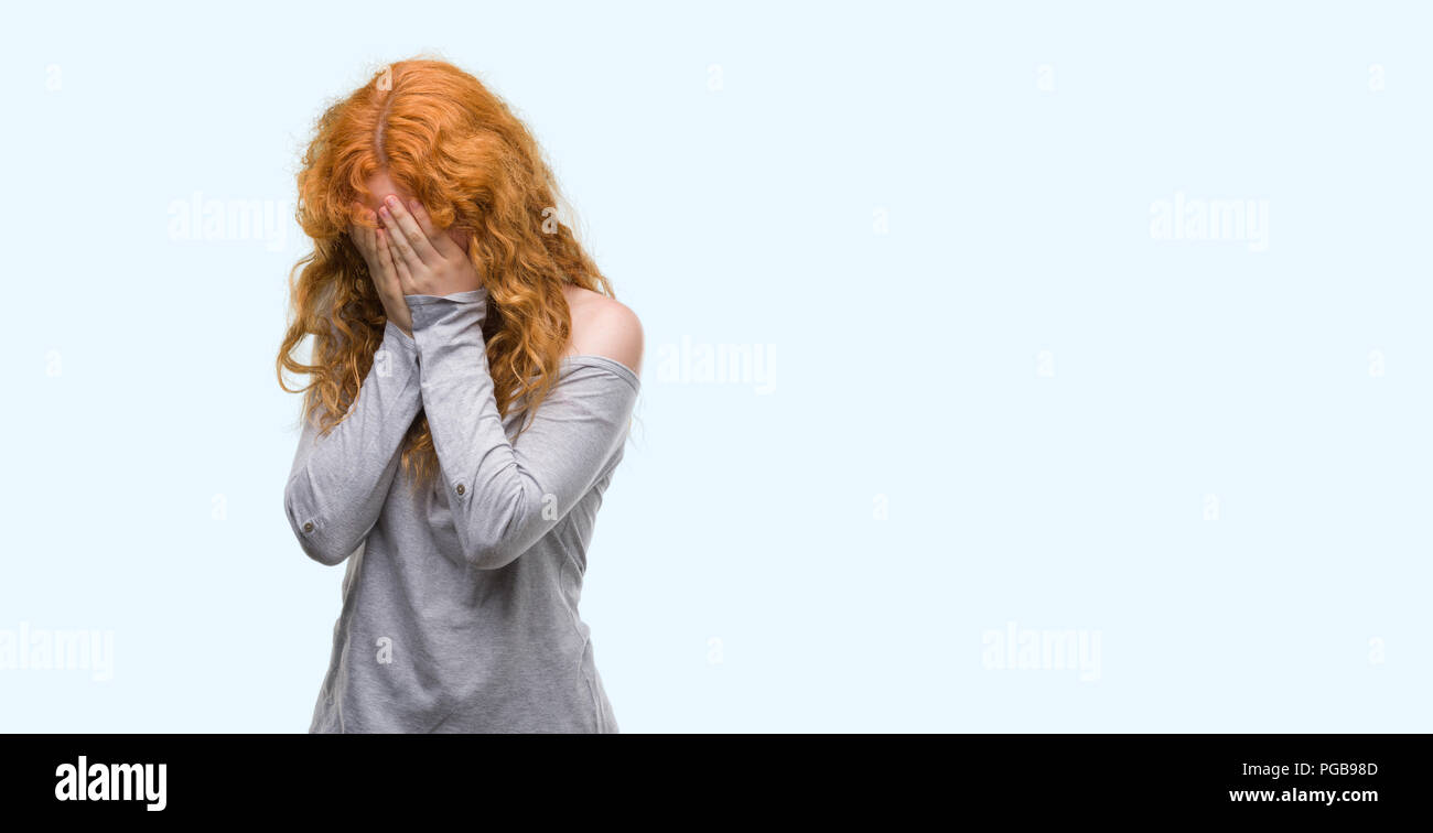 Young redhead woman with sad expression covering face with hands while ...