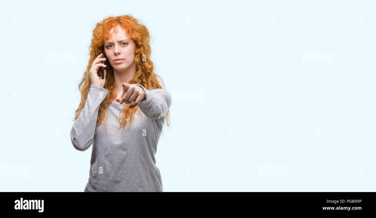 Young redhead woman talking on the phone pointing with finger to the ...