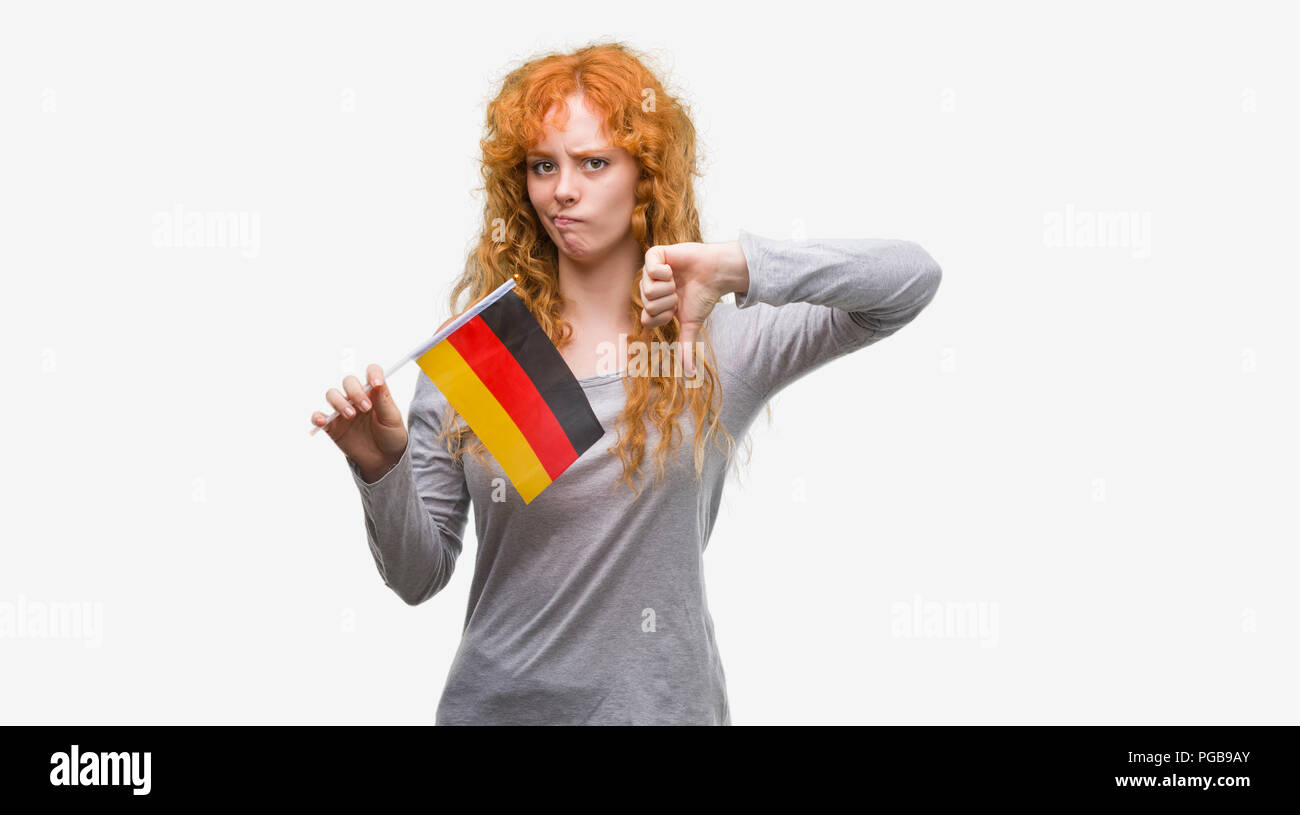 Young redhead woman holding flag of Germany with angry face, negative ...